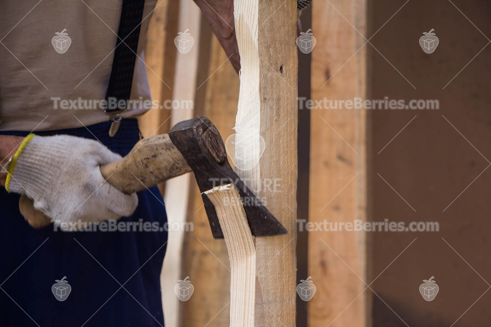 A carpenter with ax planing wood plank