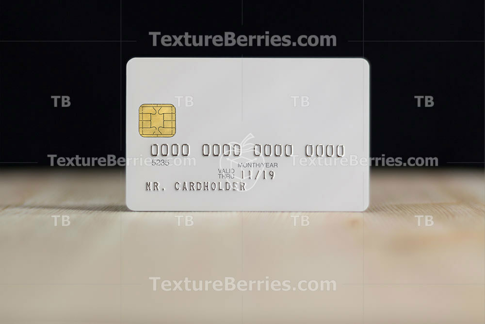 White credit card with embossing on wooden table over black wall